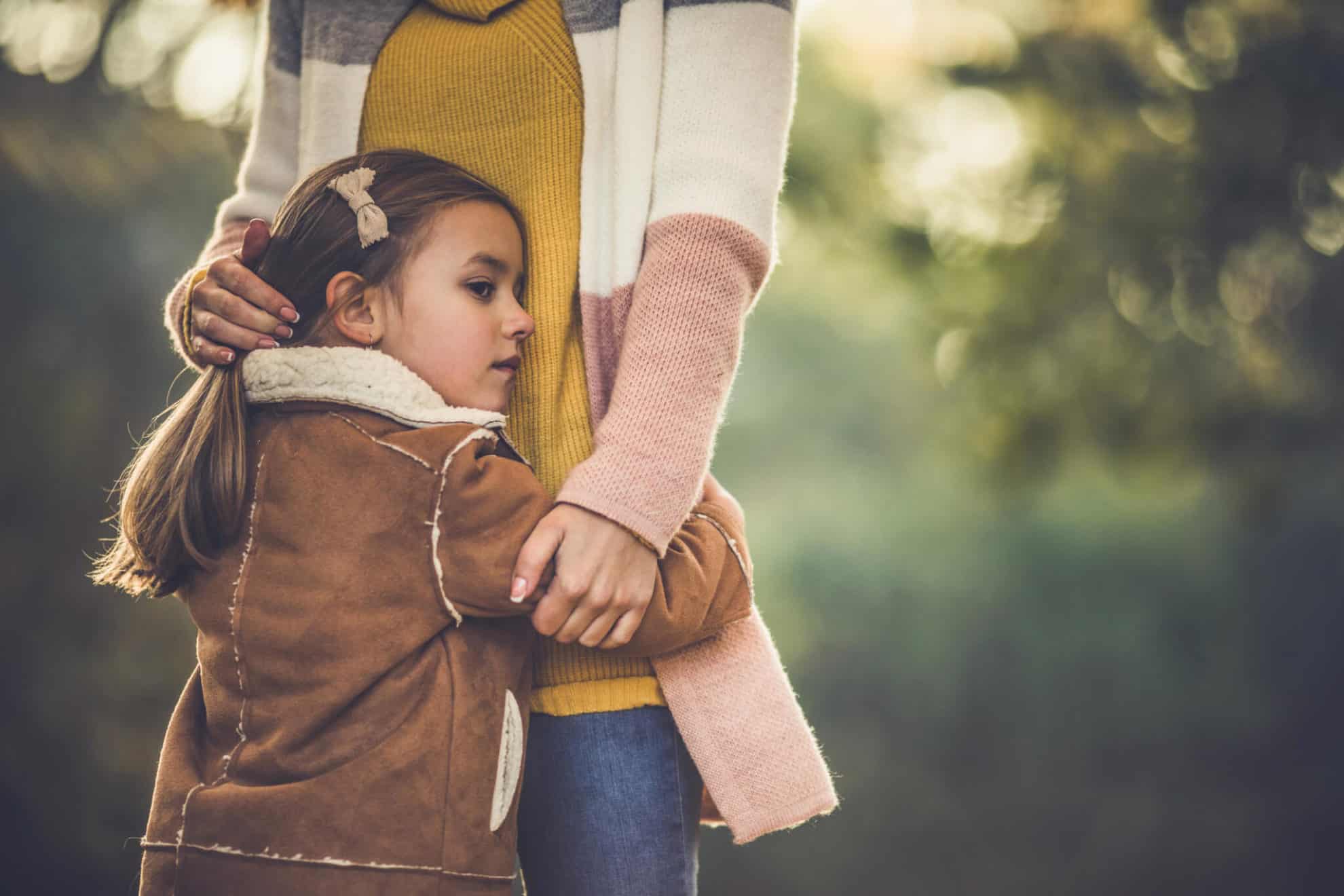 Sad little girl embracing her mother in nature. | Considering Adoption